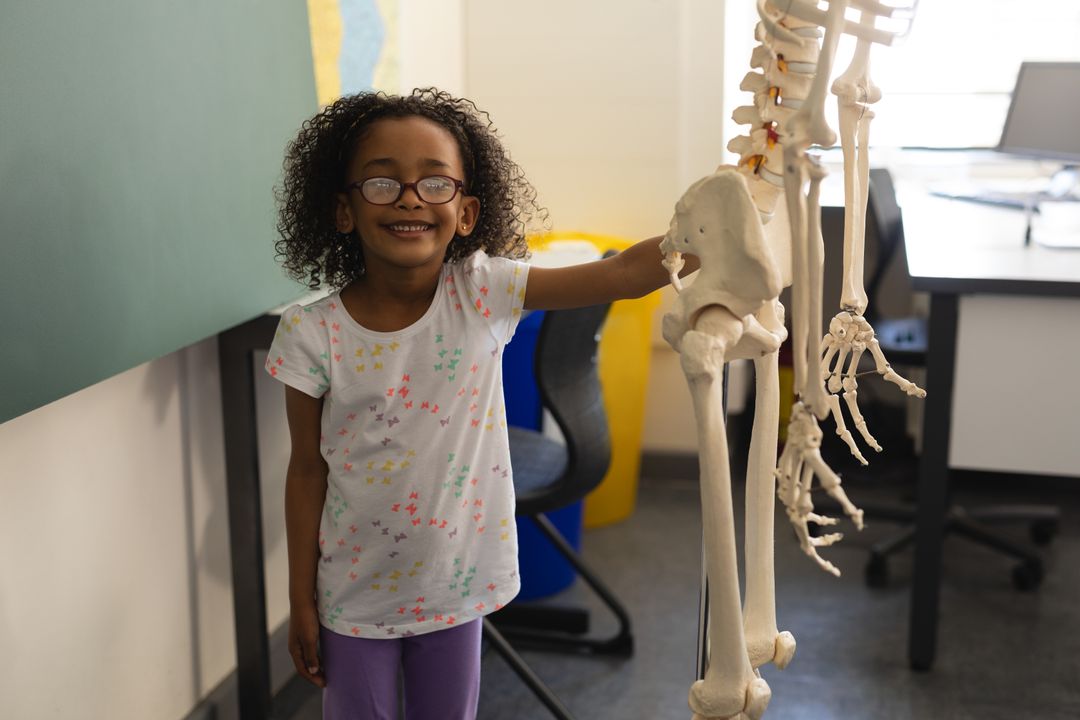 Smiling Schoolgirl Examining Skeleton Model in Classroom
