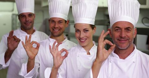 Four cheerful chefs looking making ok sign in a commercial kitchen from ...
